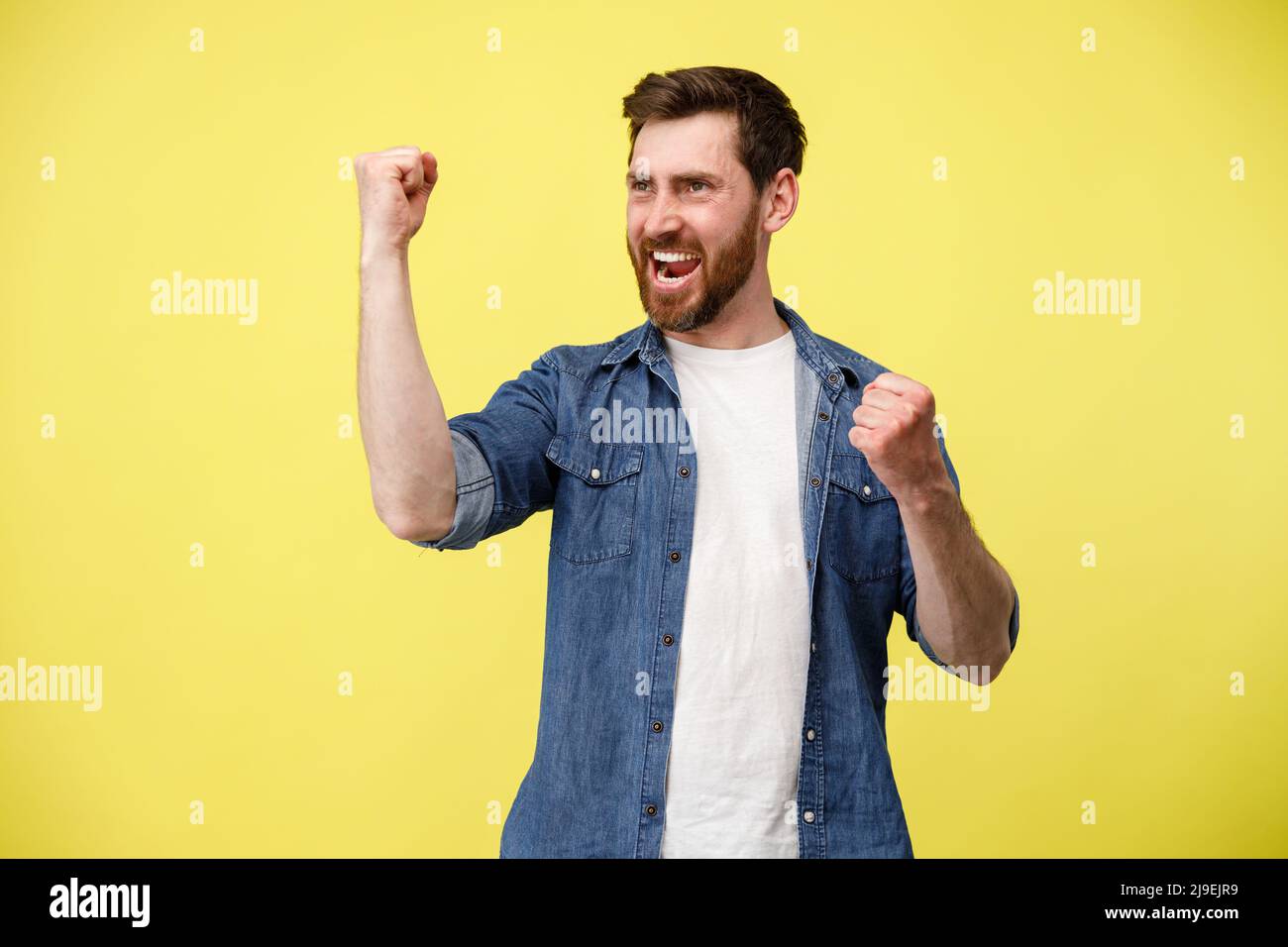 Happy joyful man doing winner gesture clenching fists and looks at side ...