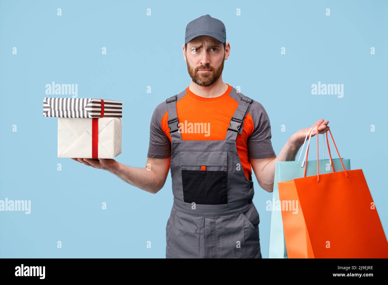 Sad male courier in uniform holding shopping bags and gift boxes on ...