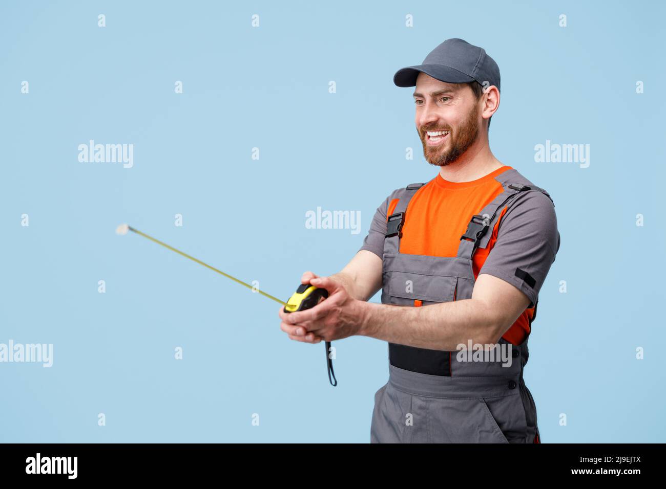 Smiling builder worker holding and looks on measuring tape tool. Studio ...