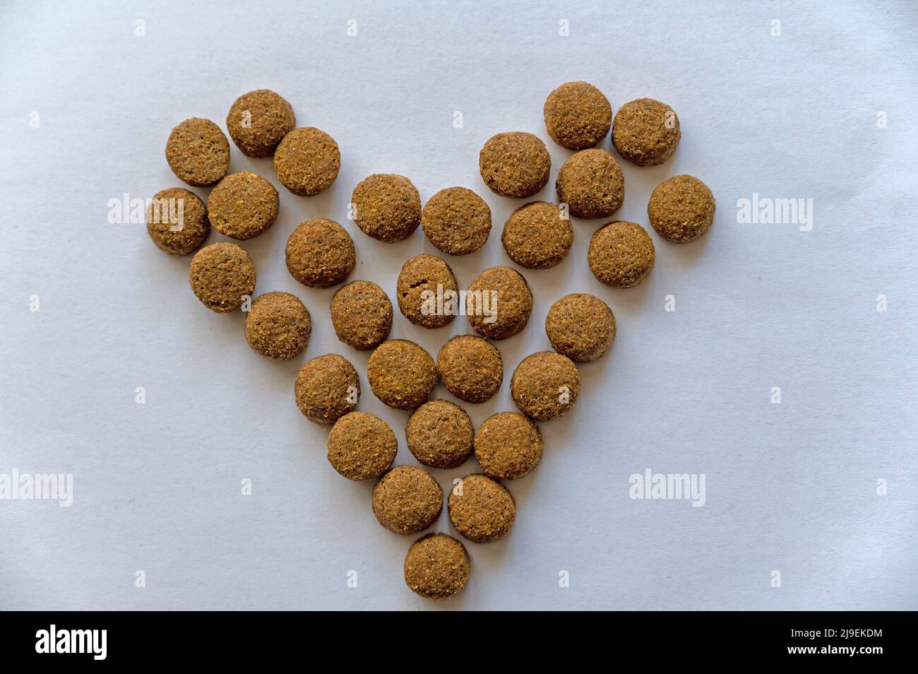 Dry pelleted pet food lined in a heart shape. Round brown pellets ...
