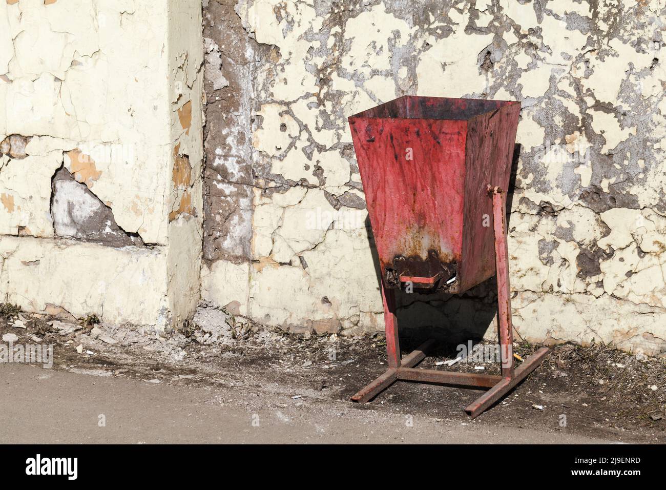Rusty red trash can stands near grungy old concrete wall Stock Photo ...