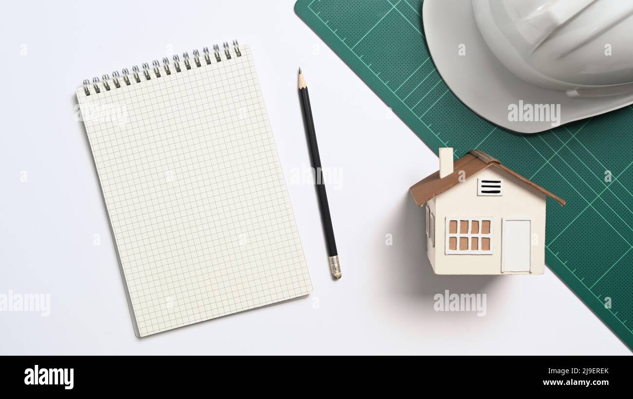Above view blank notebook, house model and safety helmet on white table ...