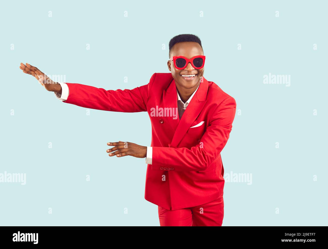 Cheerful African man in funky red suit and sunglasses dancing isolated ...