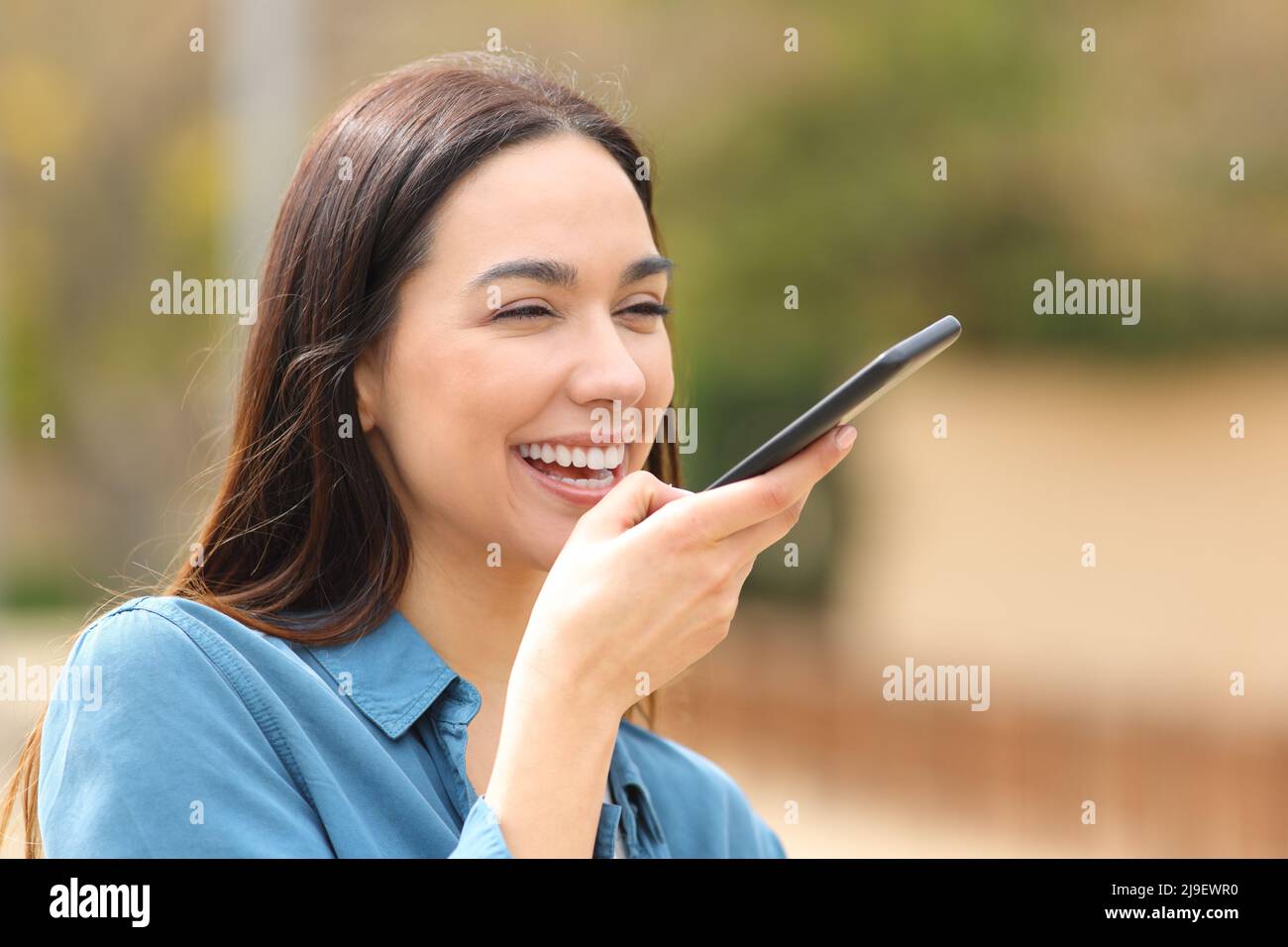 Happy woman dictating message using voice recognition in the street on ...