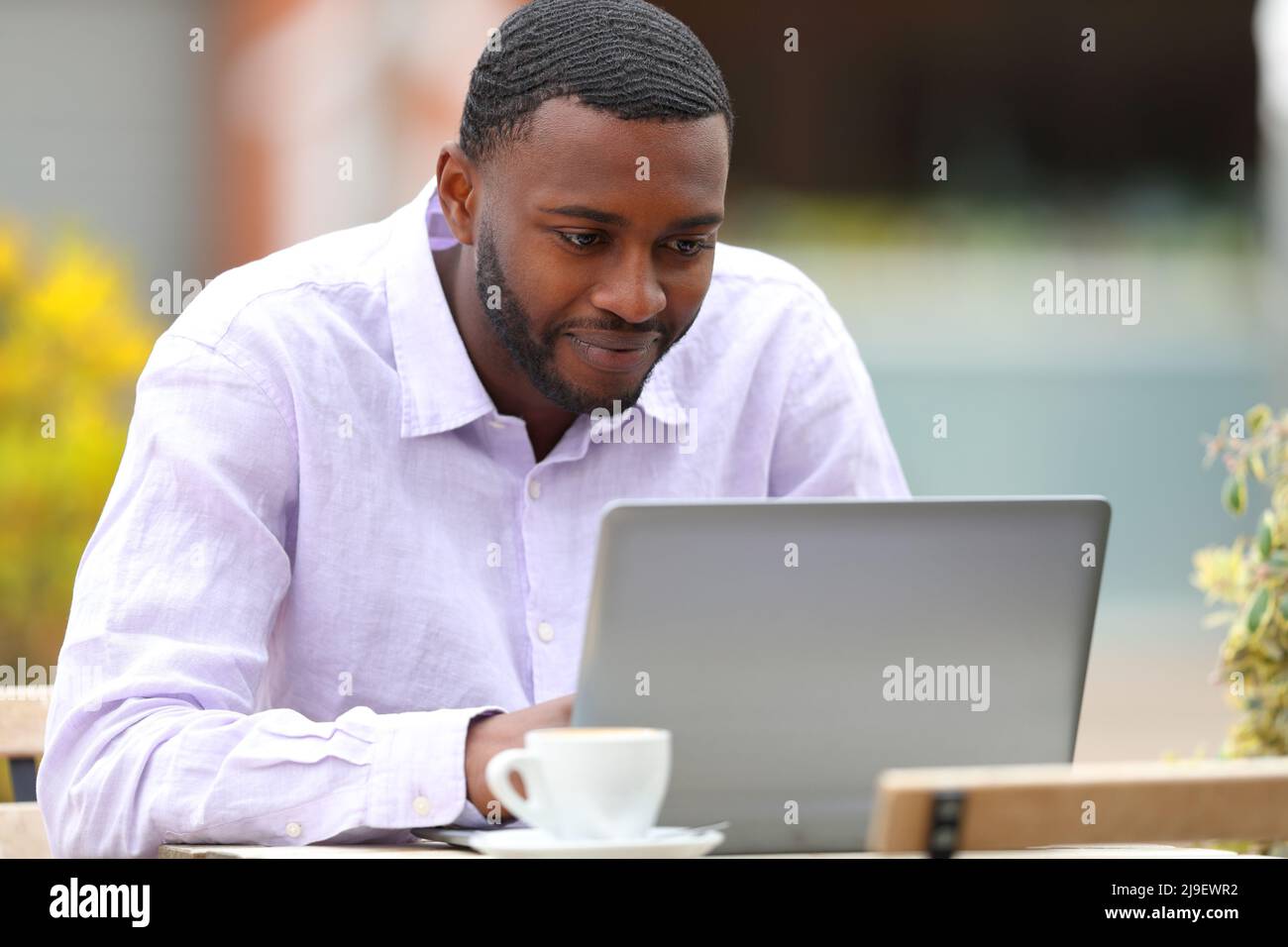 Satisfied man with black skin using laptop in a coffee shop terrace ...