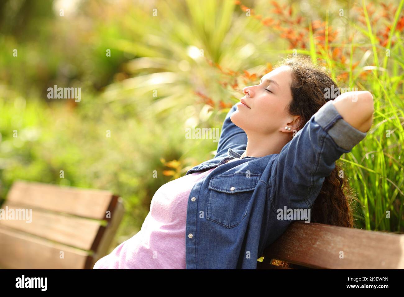 Profile of a woman relaxing and resting sitting in a bench in a park ...