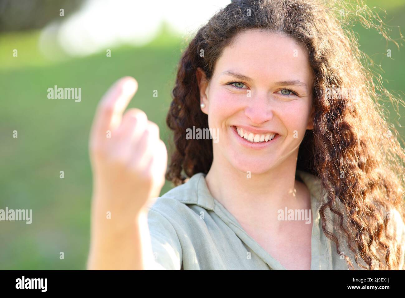 Front view portrait of a happy candid woman saying come here in a park ...
