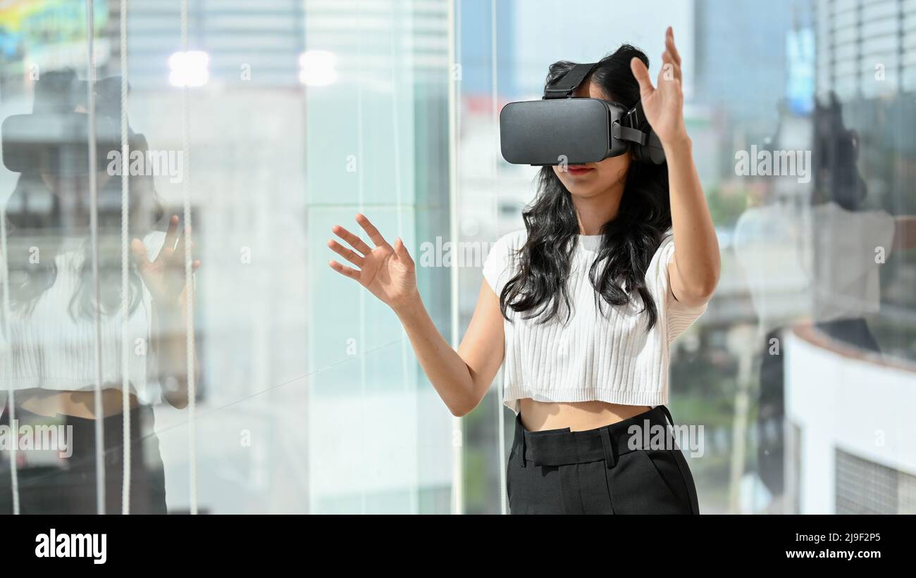 Beautiful Asian millennial woman wearing a VR headset, playing a ...