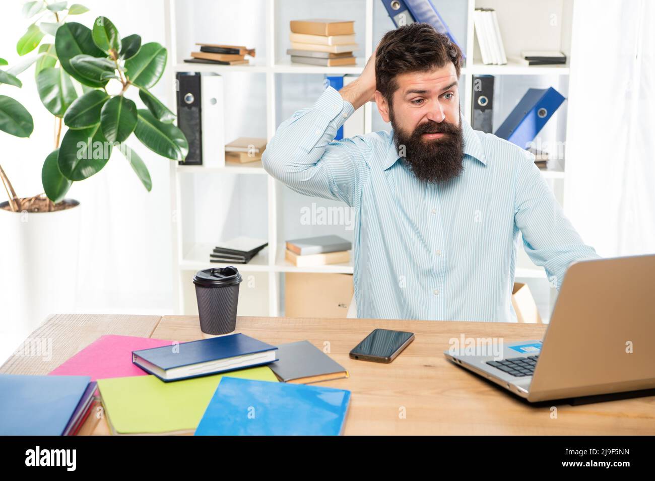 Confused businessman scratching head while working at laptop in office ...