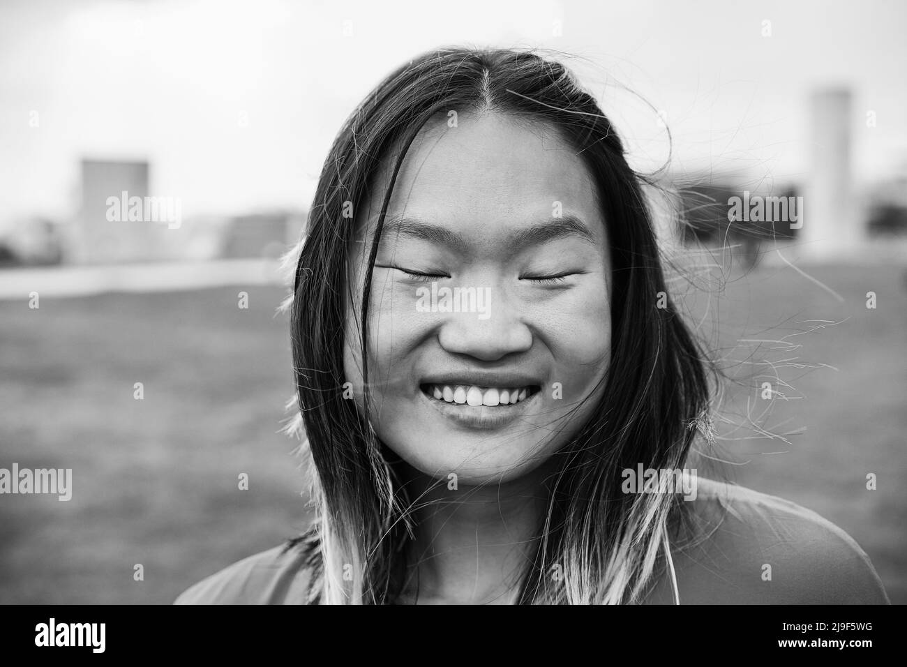 Asian girl smiling on camera at city park - Focus on face - Black and ...