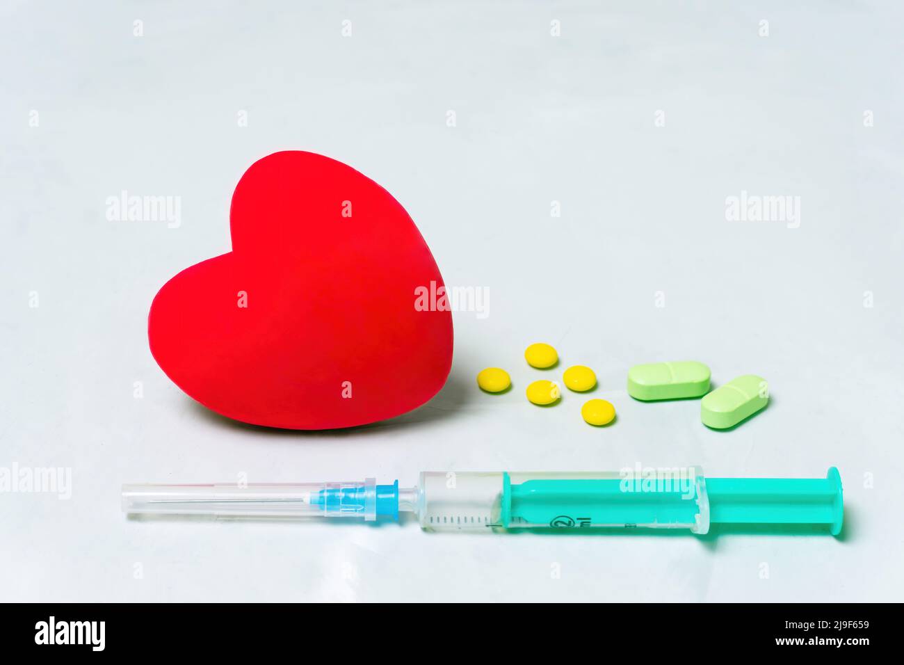 Large red heart shape, syringe and pills on a gray background with copy ...