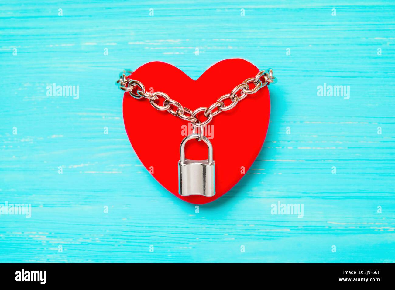 Big red heart in chains with a miniature padlock on a turquoise wooden ...