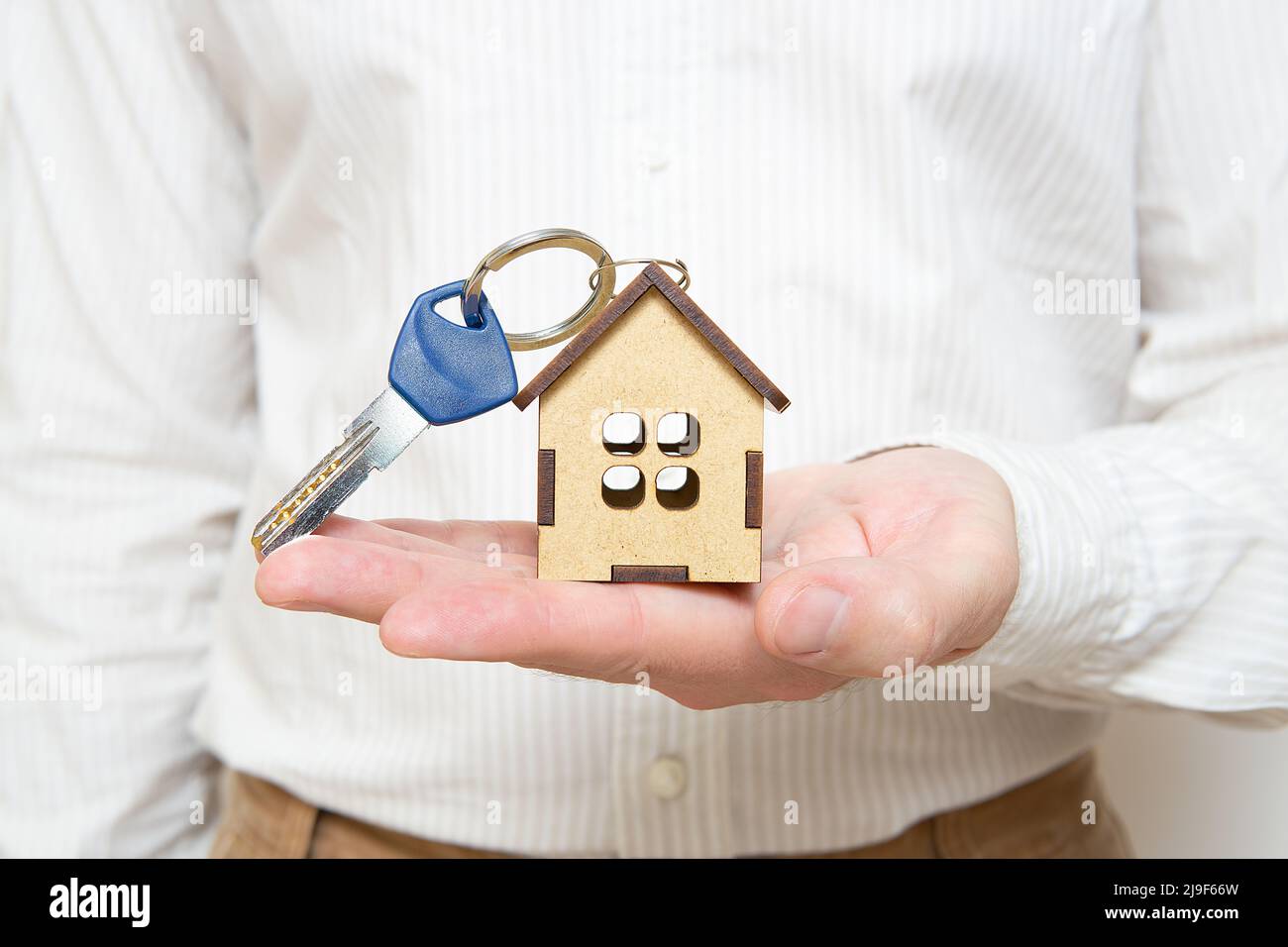 Man holding a house key with a miniature wooden house model keychain ...
