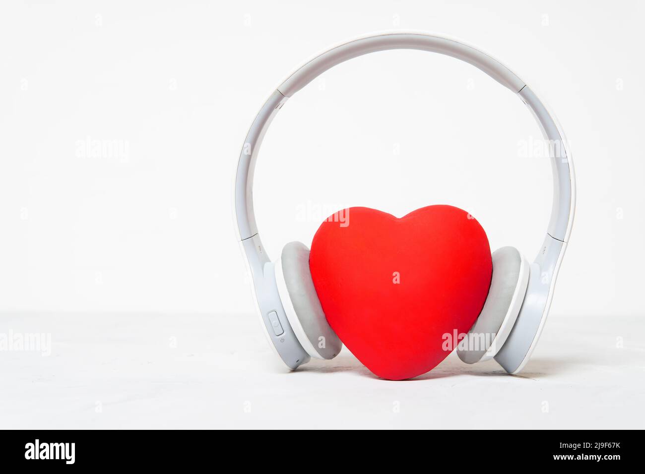 Wireless headphones over a large red heart shape isolated on a neutral ...