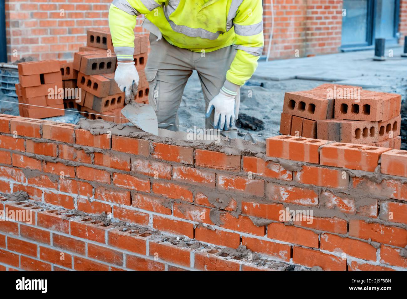 Bricklayer in safety vest and a helmet laying a brick wall using a ...