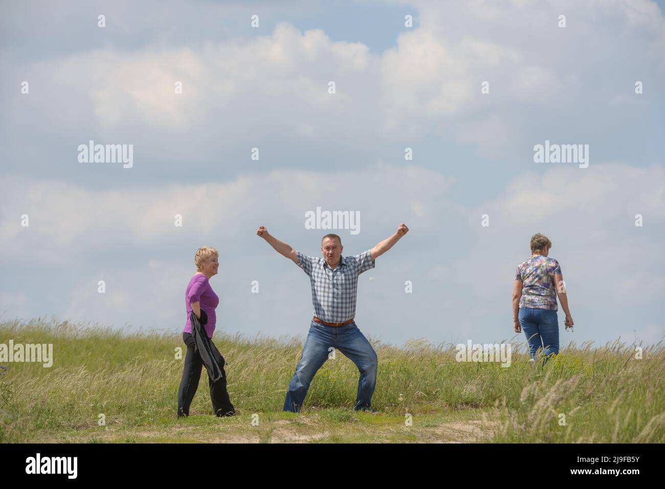 Elderly man is funny gesturing while walking with two women along wild ...