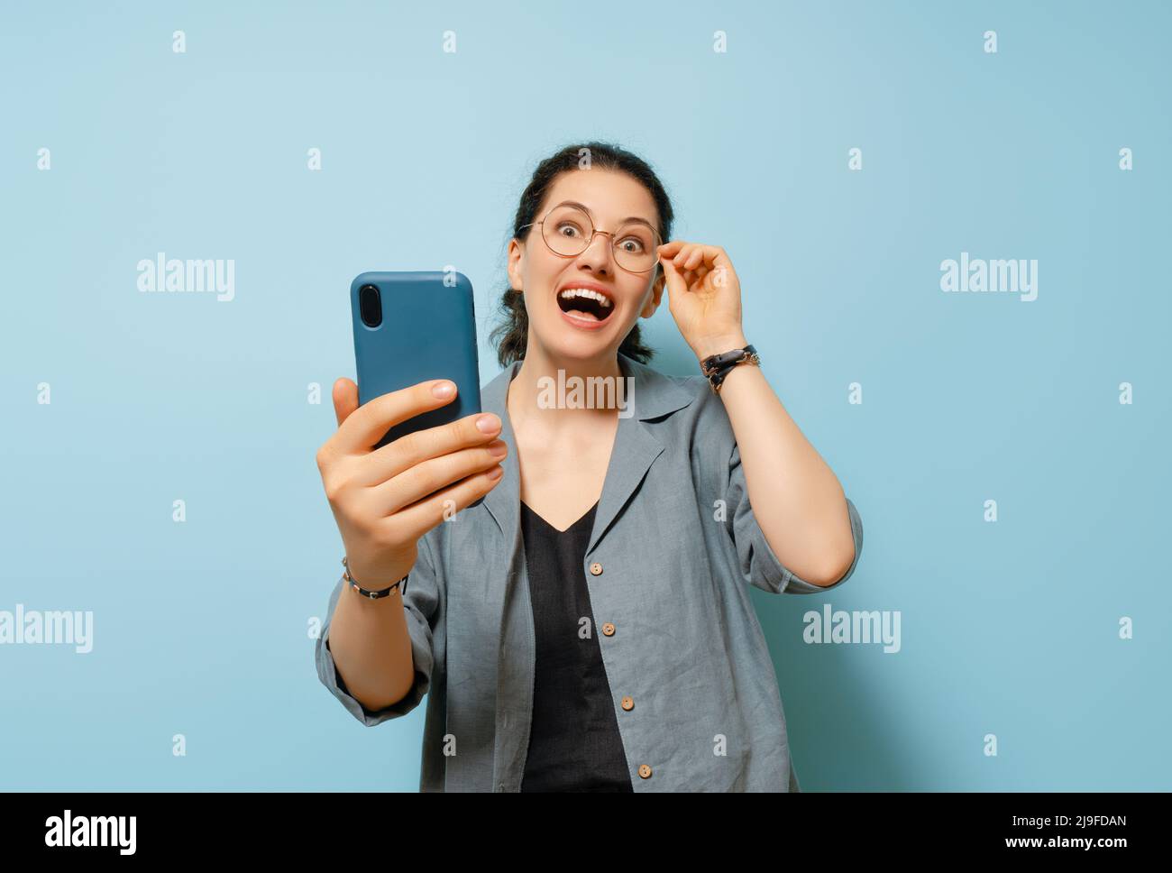 Happy young woman with smartphone on background of blue wall Stock ...