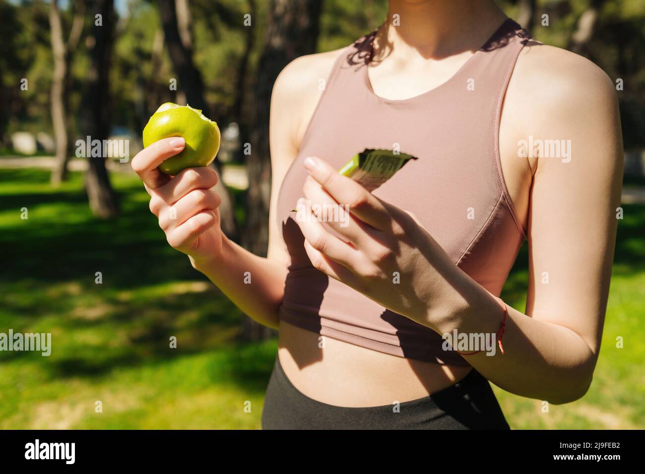 Beautiful sporty woman eating apple and holding protein bar while ...