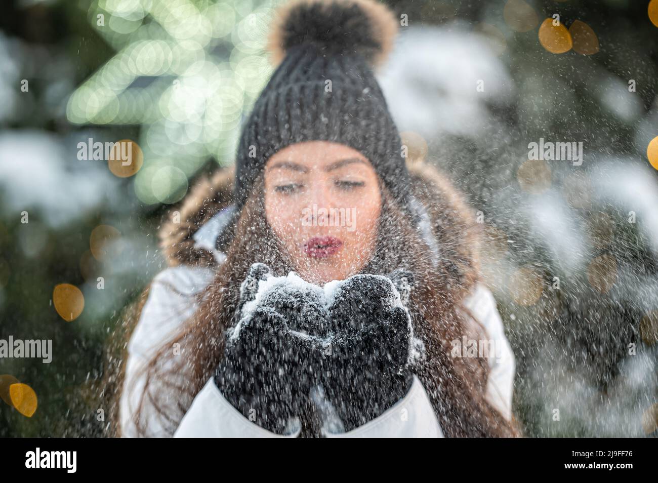 young woman blows snow from her hands while standing against the ...