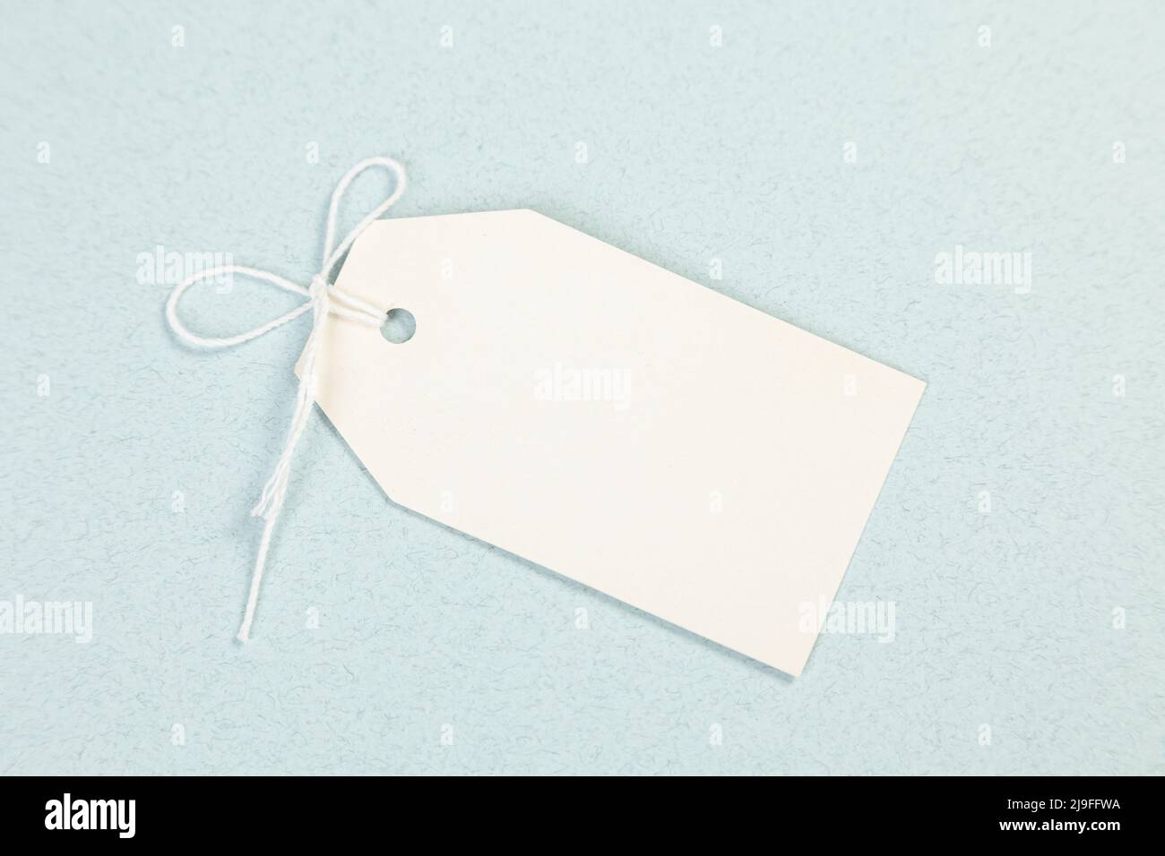 An empty white price tag lies on a gray-blue background with a soft ...