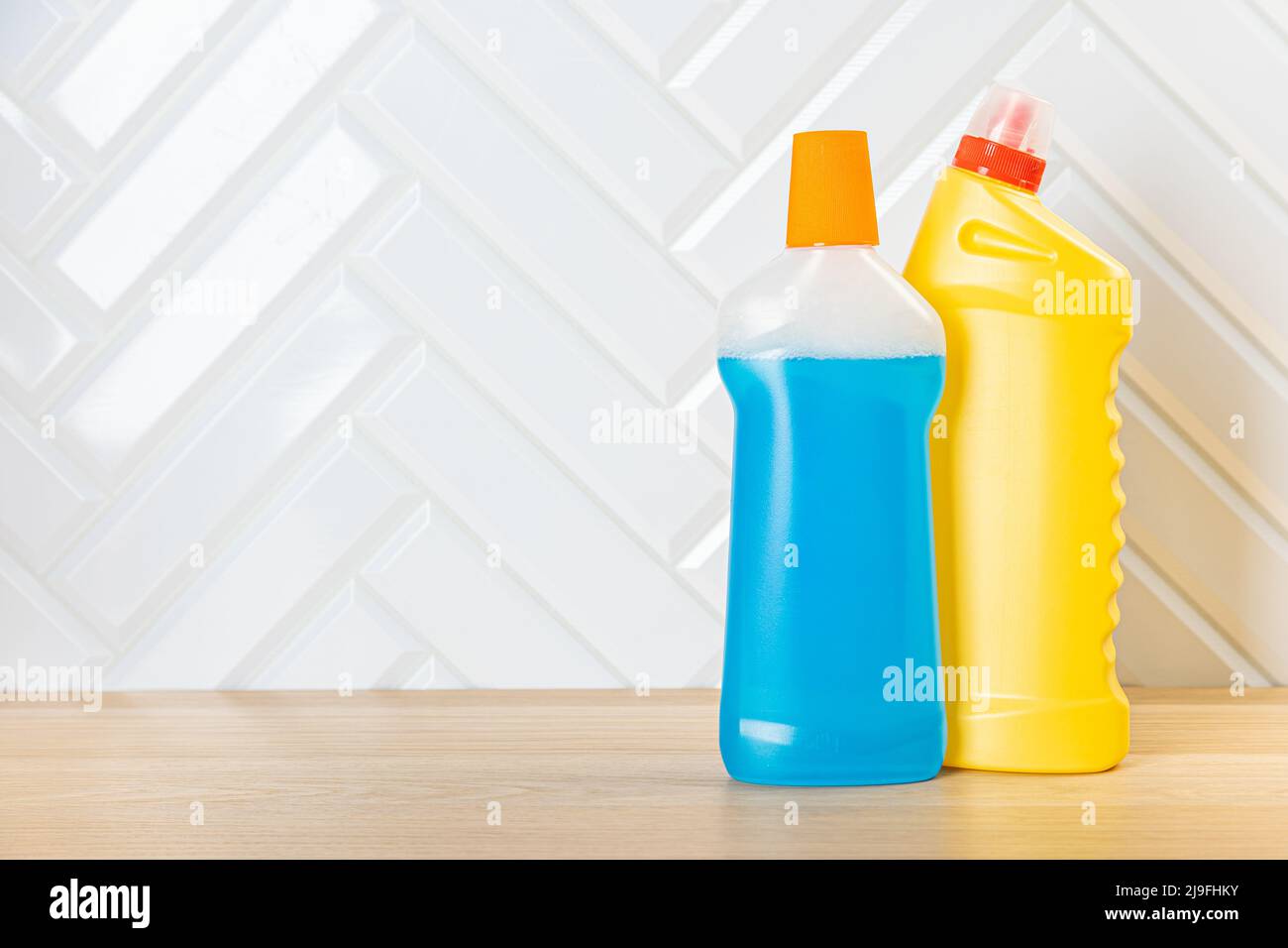 Bottles with detergent and cleaning supplies on wooden table and light ...