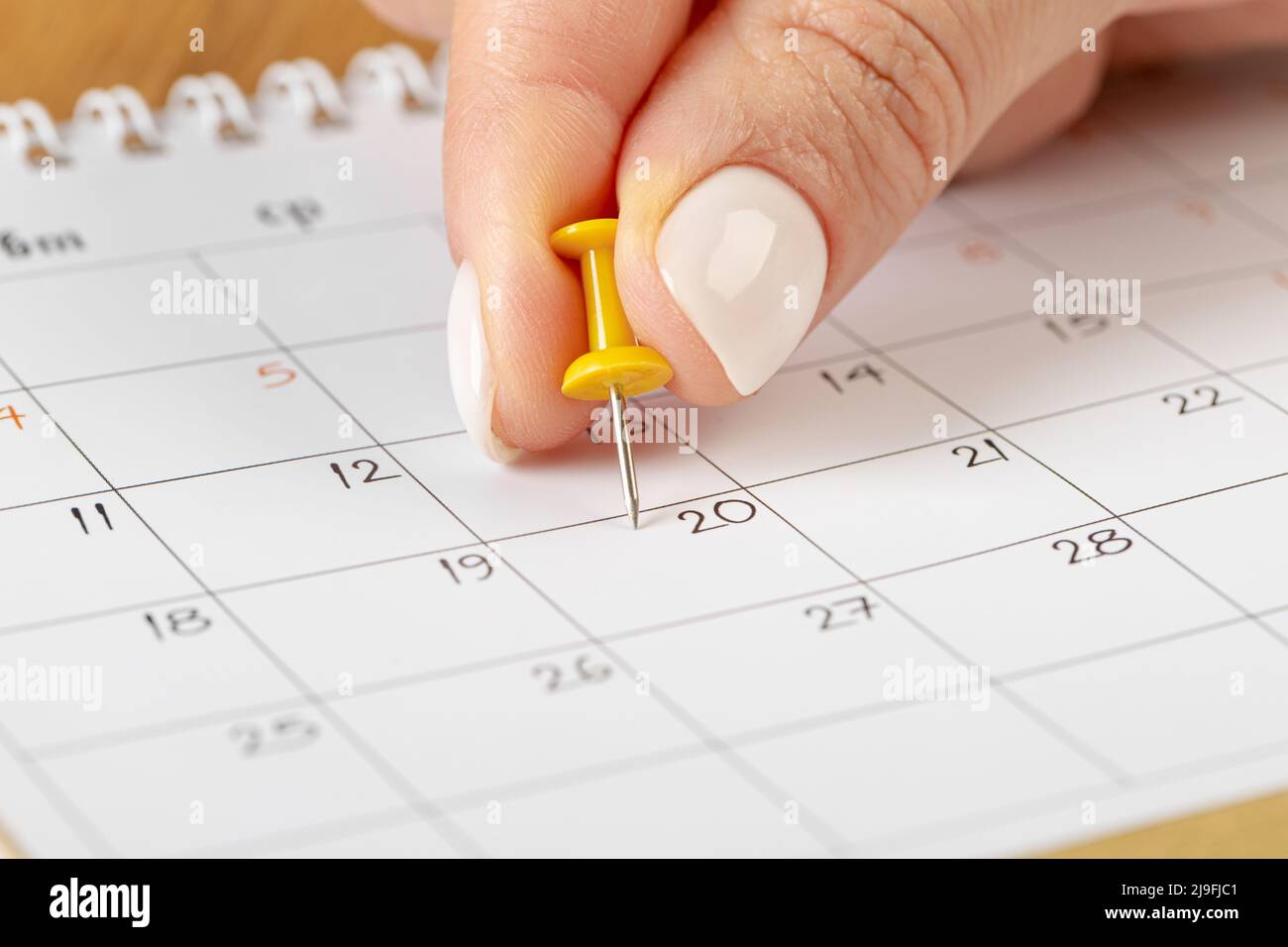 a female hand with a beautiful manicure holds a yellow pushpin to mark ...