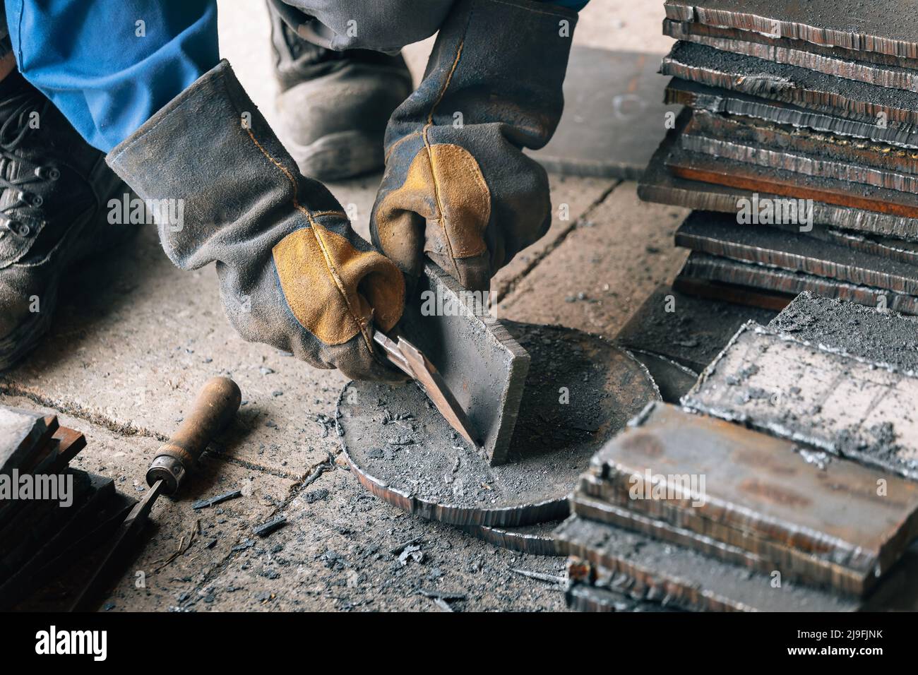Worker in heavy industry or metallurgy beats scale off iron plates with ...