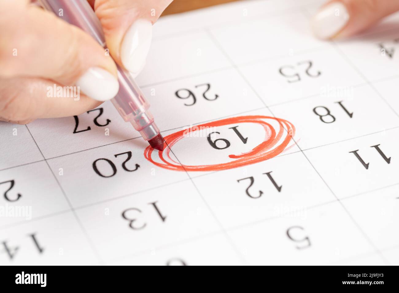 female hand marking with a red pen on a calendar circles the day ...