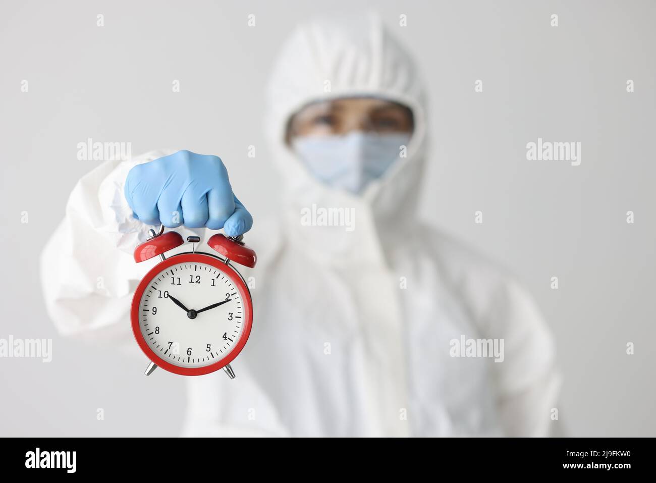 Person in protective suit with glasses and mask holds alarm clock Stock ...
