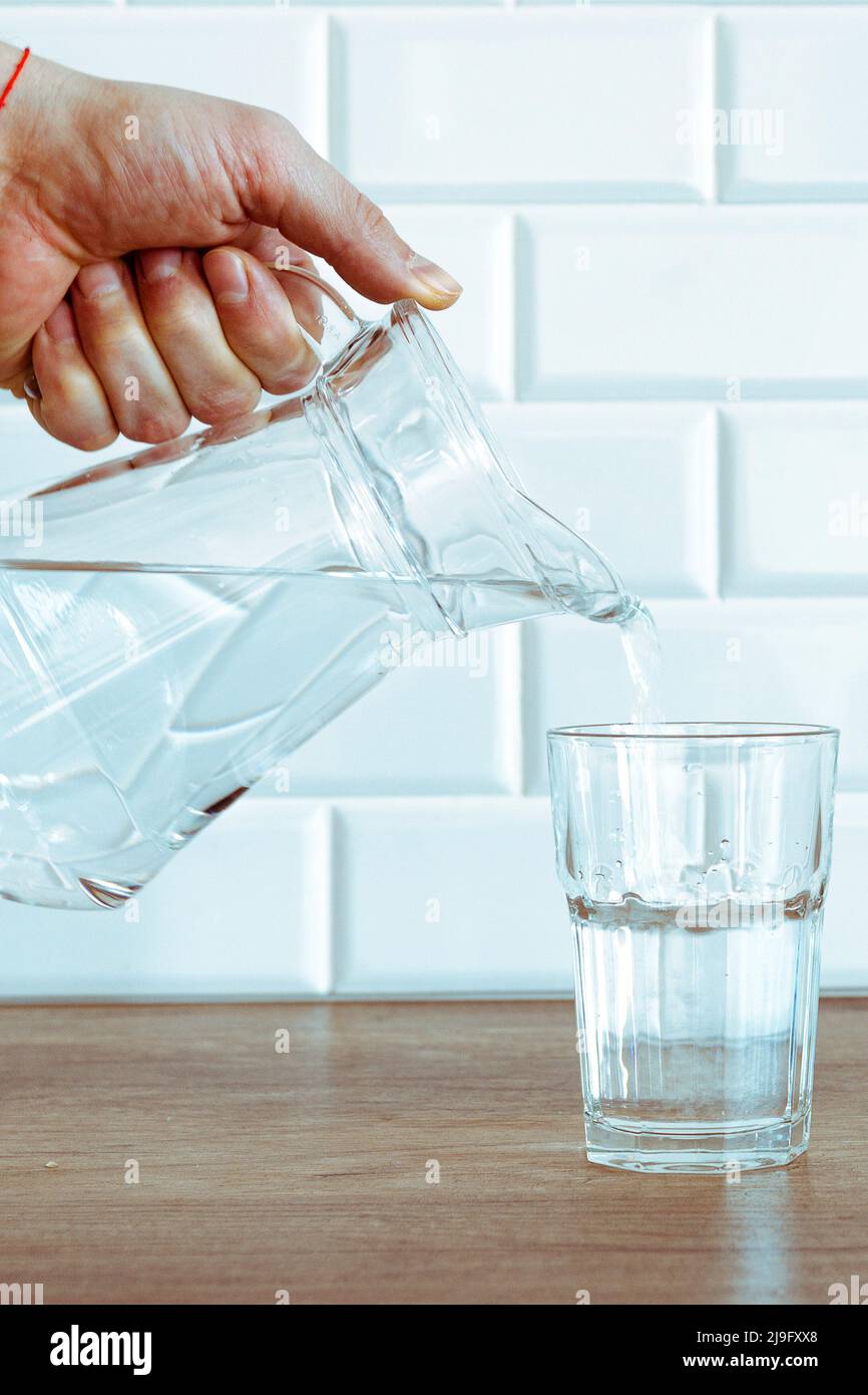 A man's hand pouring fresh pure water from bottle into a glass on the ...