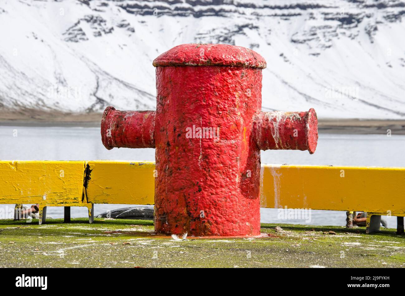 A red, rusty steel bollard and a yellow wooden beam on a quay in a ...