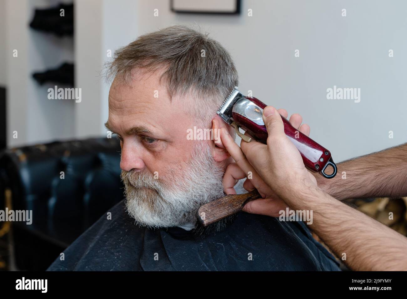 An old man enjoing haircut by a master in a barbershop. An old man gets ...