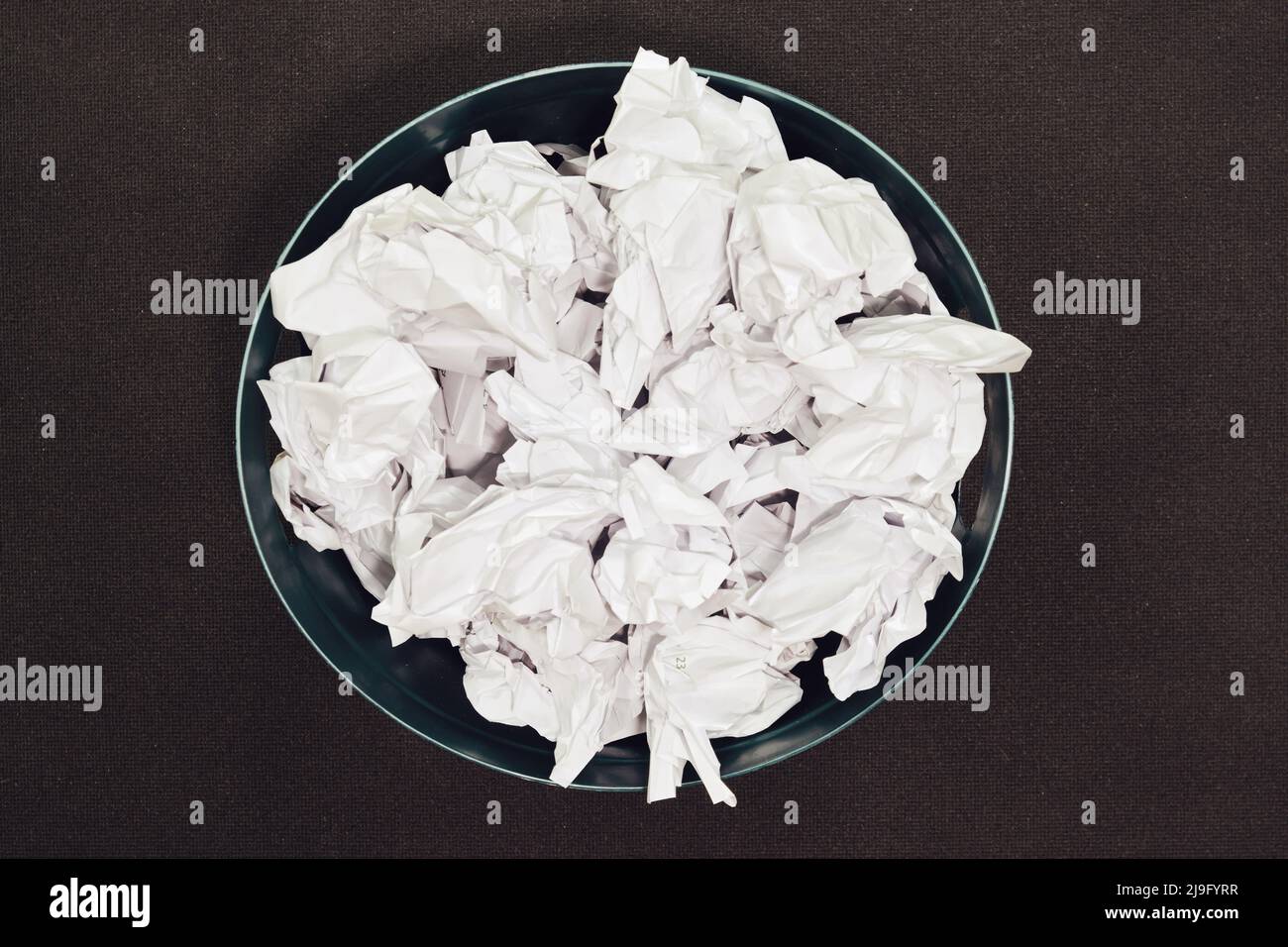 Plastic trash can being filled with crumpled sheets of white paper ...