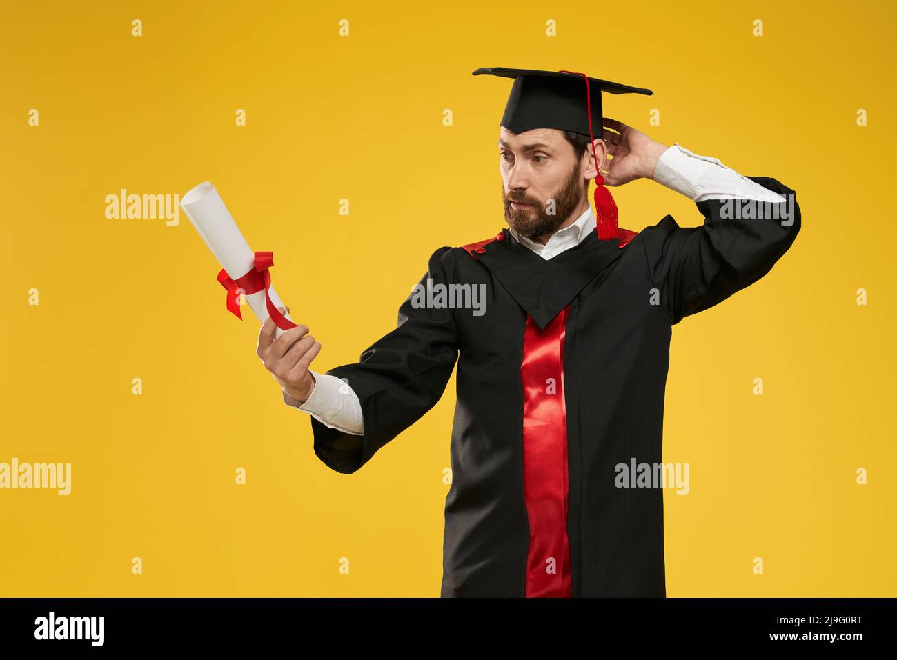 Front view of student standing, looking at diploma, mixed up, surprised ...