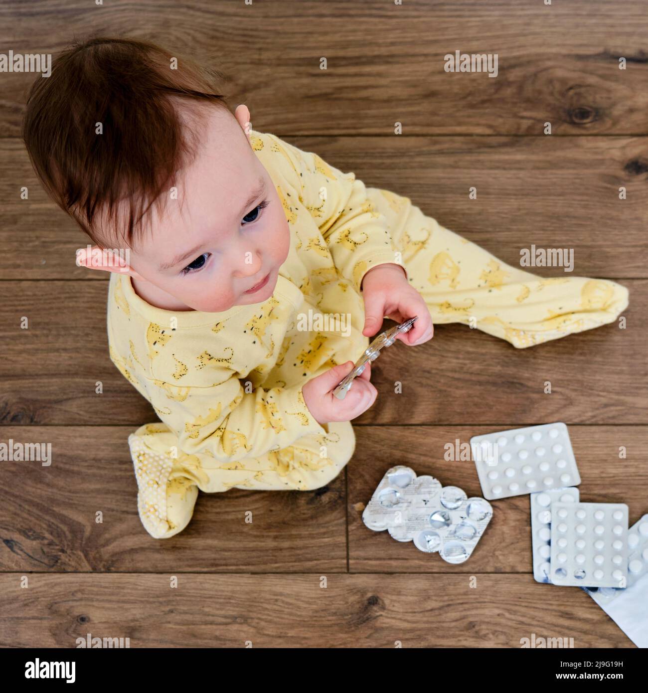 Toddler baby boy plays with medicines in a package while sitting on the ...