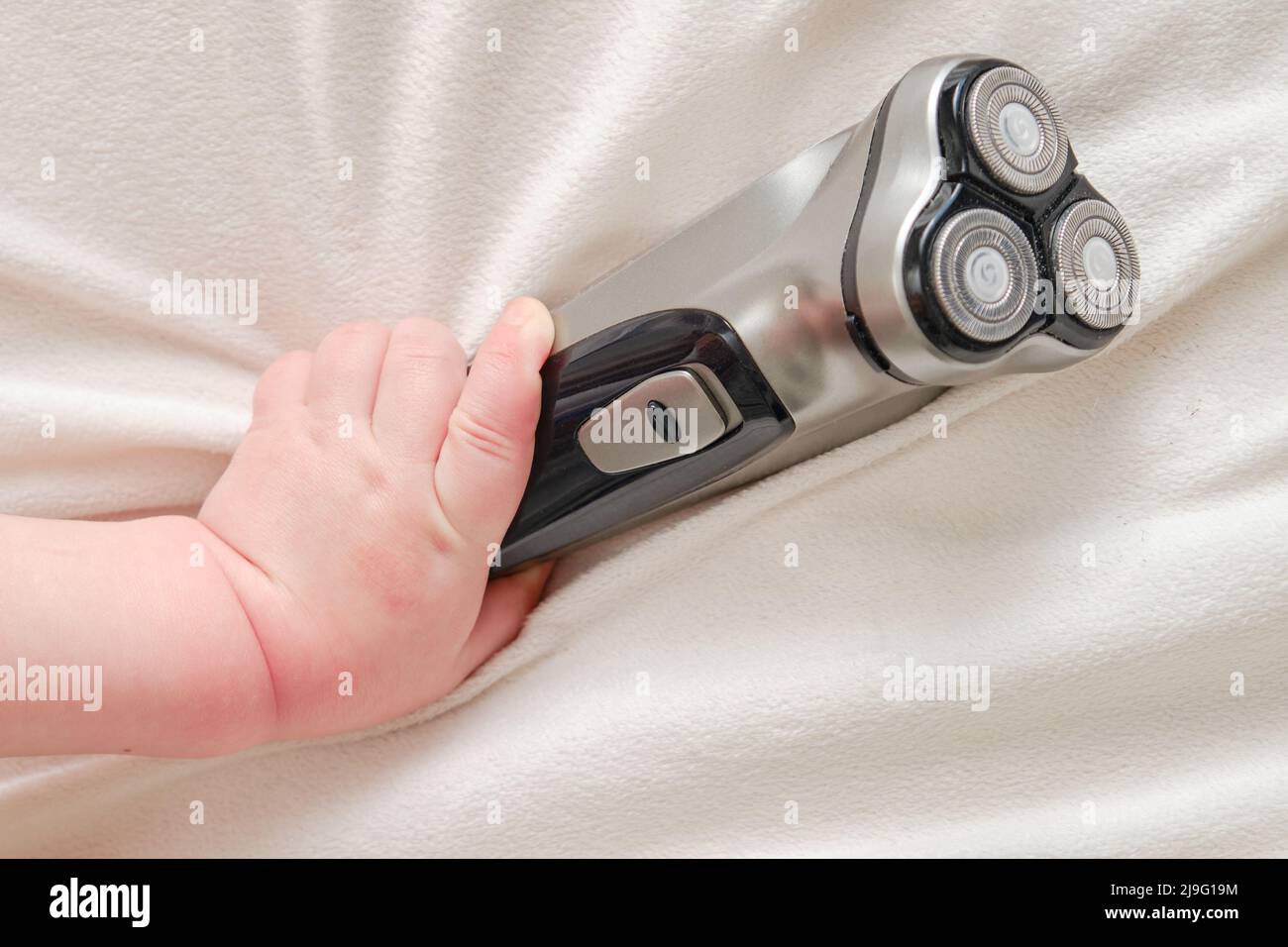 The hand of a baby toddler boy is holding an electric razor. Child with ...