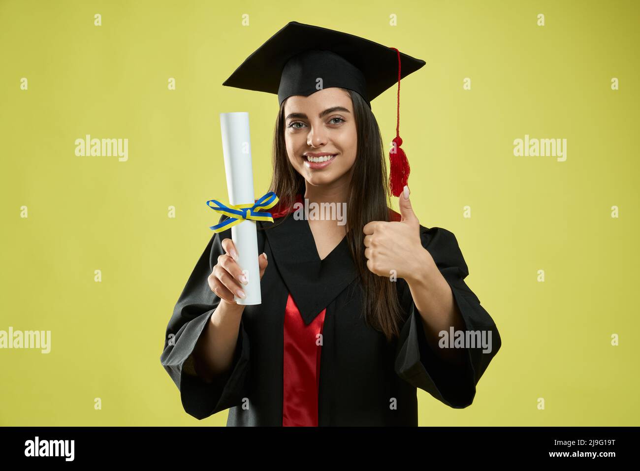 Front view of girl in mortarboard and graduate gown holding diploma ...