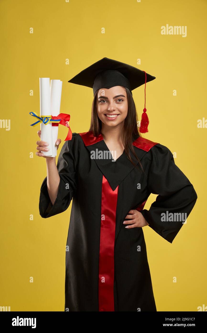 Front view of pretty female graduate standing, holding two diplomas ...