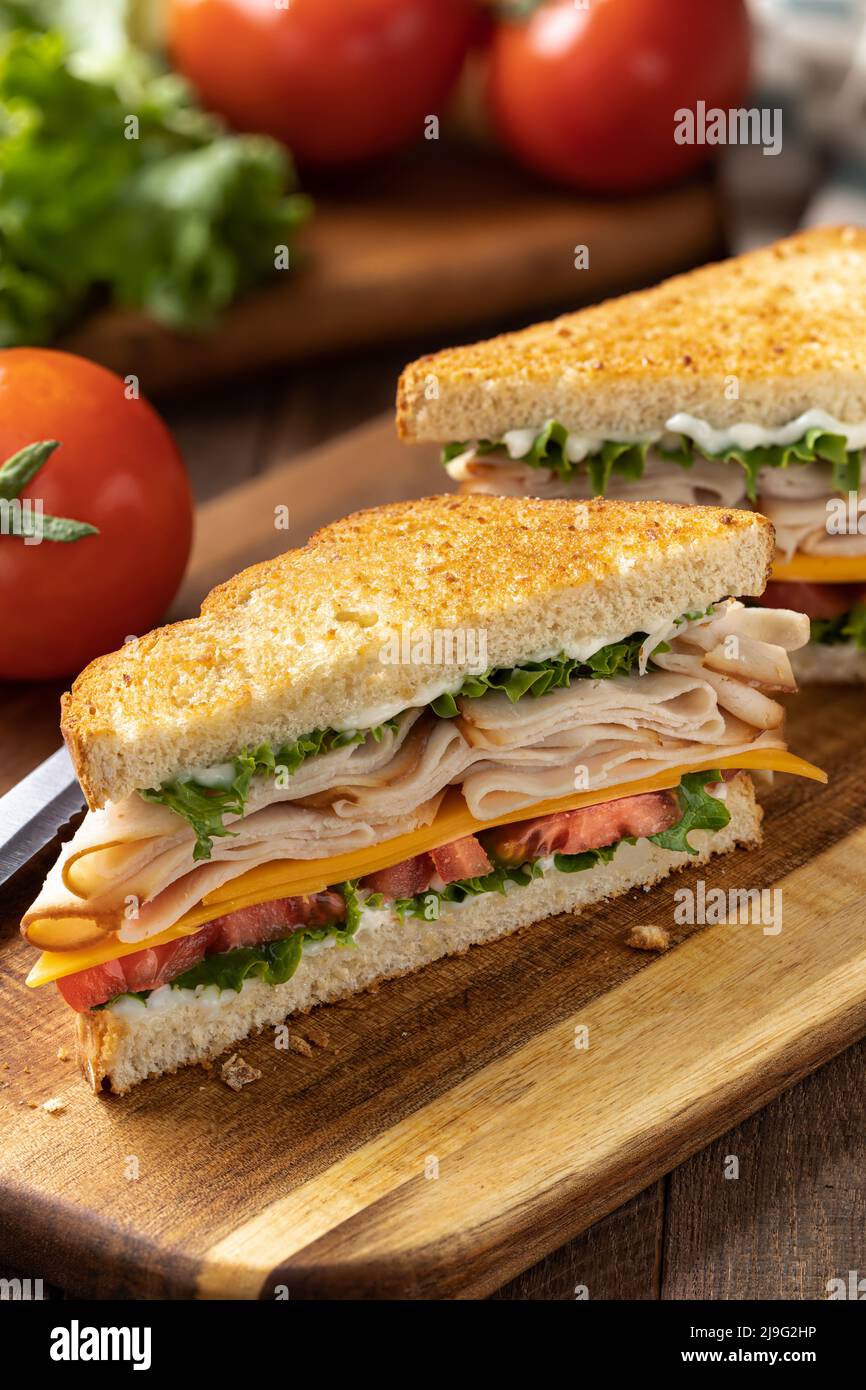Sandwich made with sliced turkey, cheese , lettuce and tomato on toasted bread cut in half on a ...