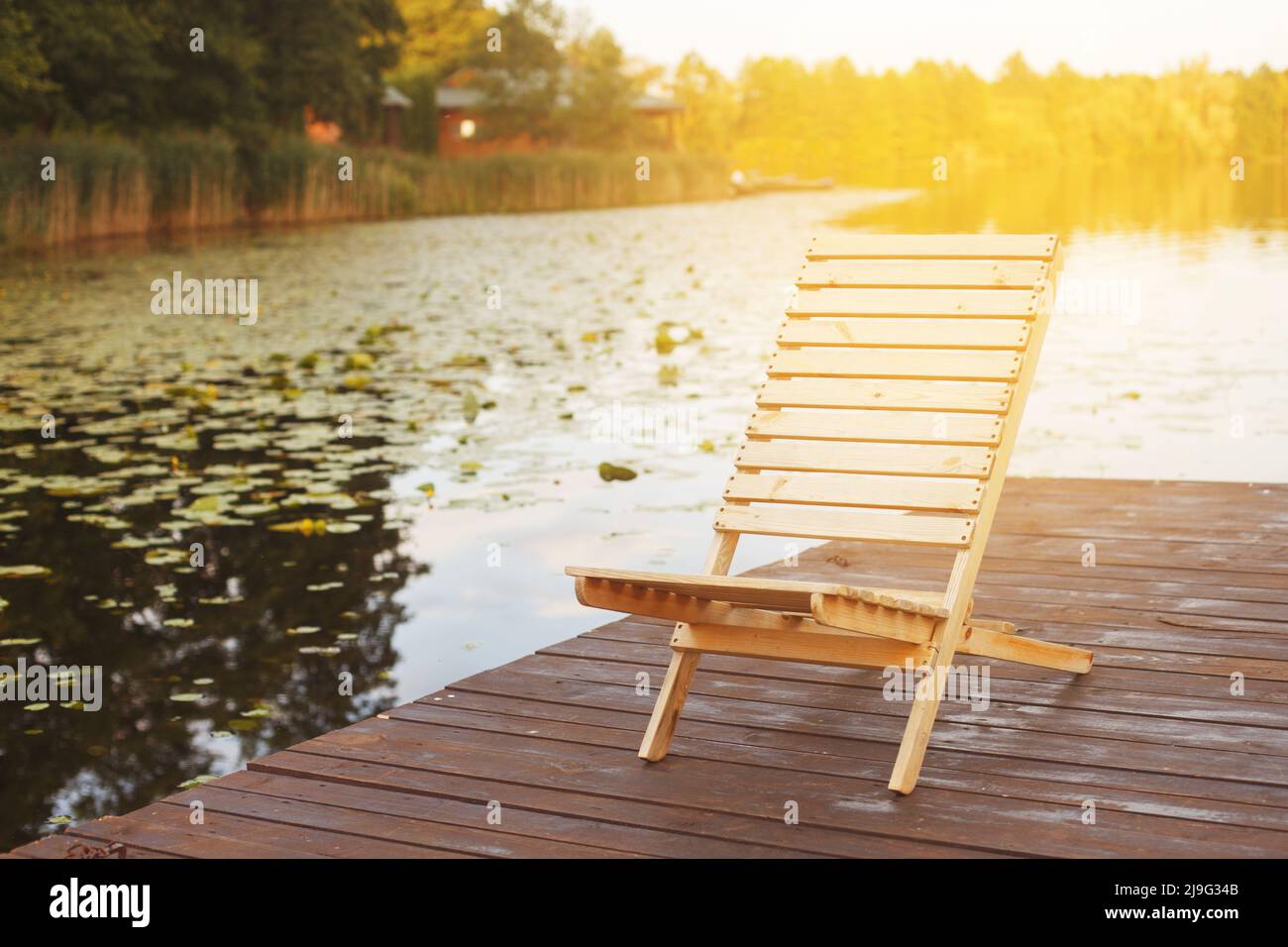 Wooden dock with lounge chair on pier on the calm lake in the middle of ...