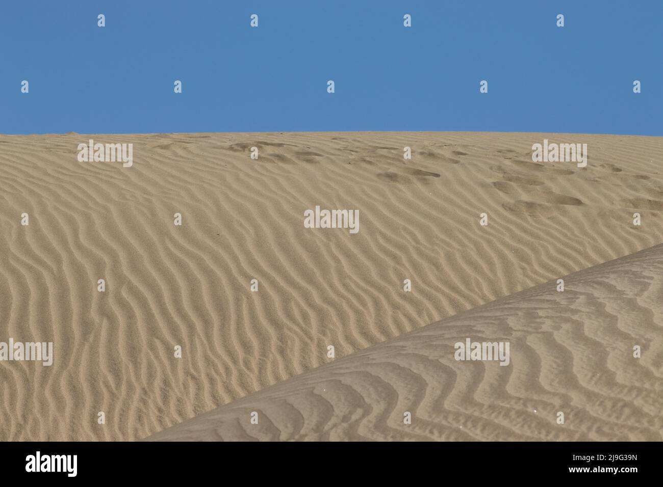 The folds of two sand dunes, showing light, texture and footsteps to ...