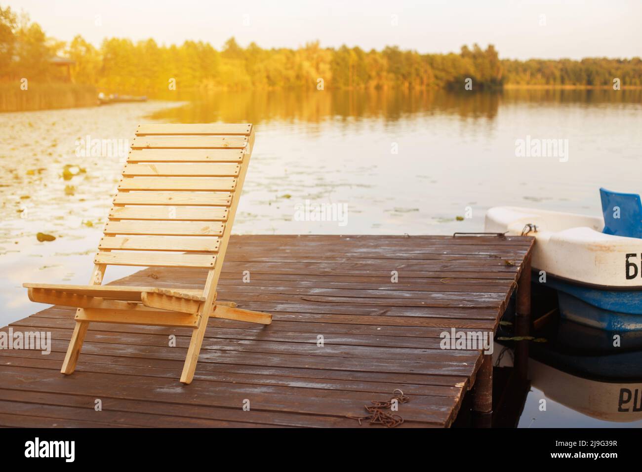 Wooden dock with lounge chair on pier on the calm lake in the middle of ...