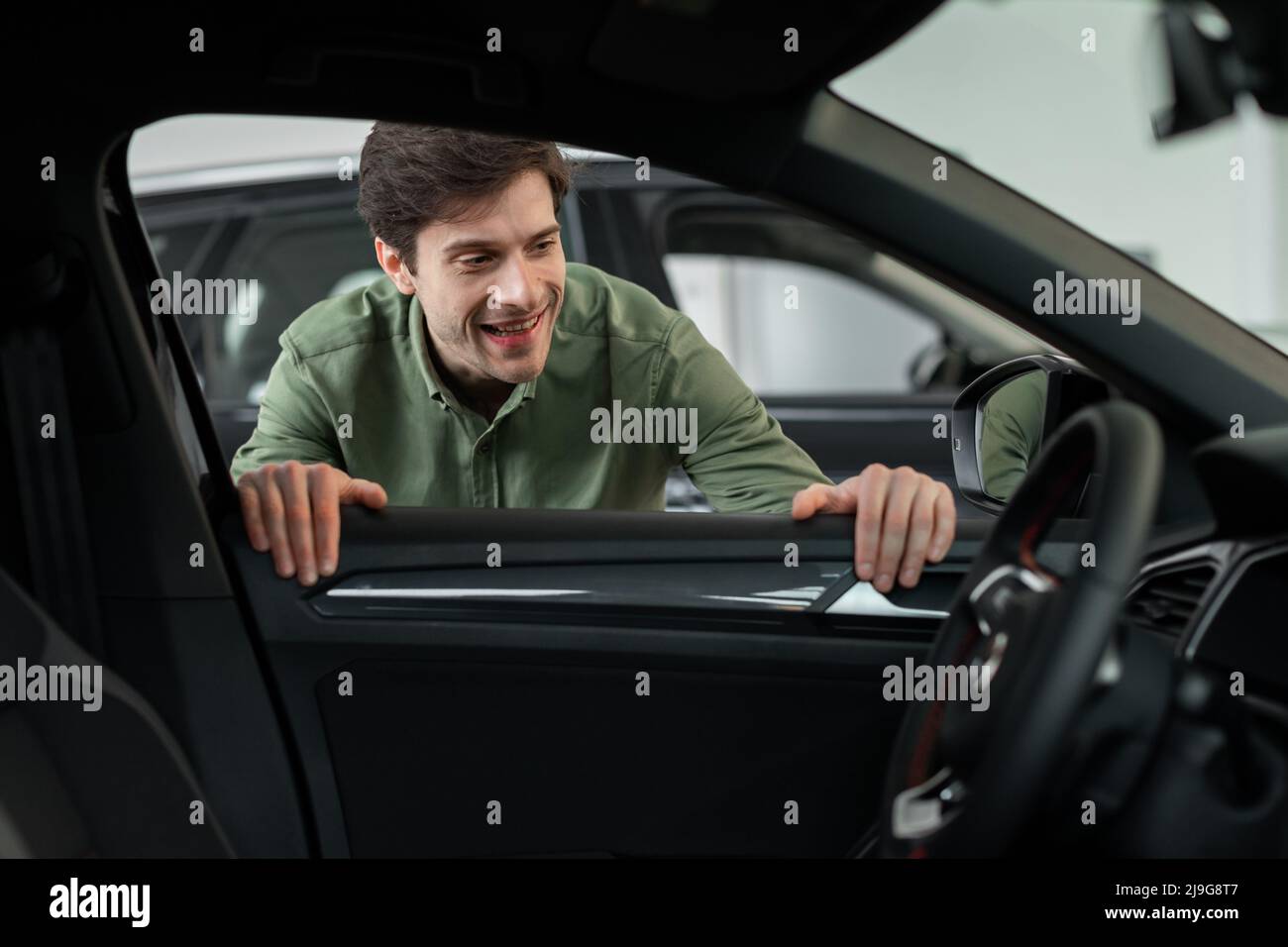 Handsome young man looking through window inside new car, checking it ...