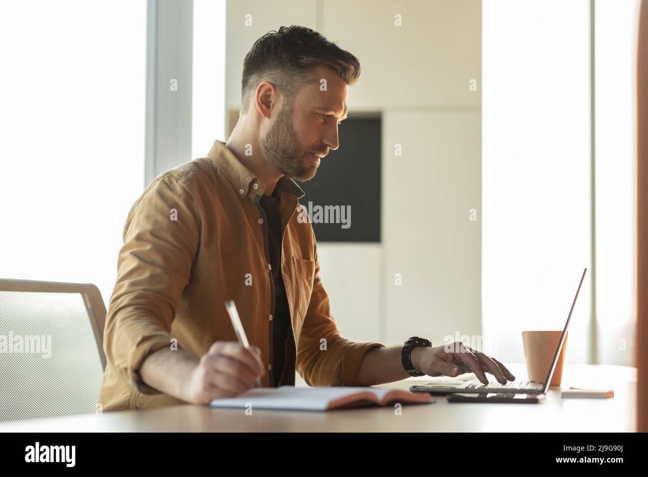 Businessman Working Using Laptop Taking Notes At Workplace, Side View ...