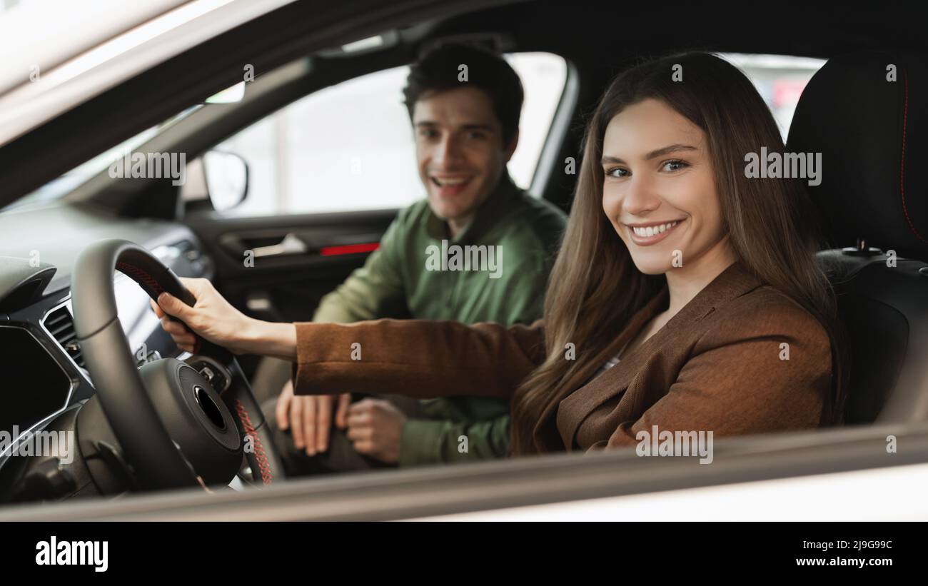 Cheery young couple sitting inside new car, checking it before purchase ...
