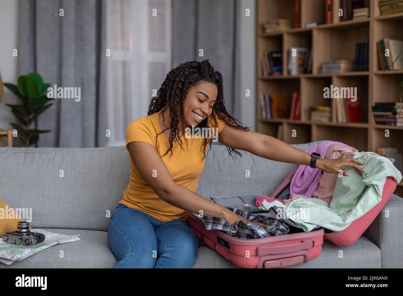 Travel preparation concept. Happy black woman packing suitcase and ...