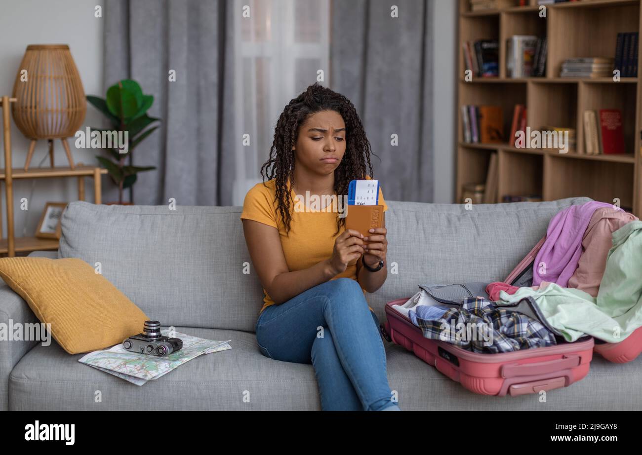 Crying black woman with travel tickets sitting on sofa with unpacked ...