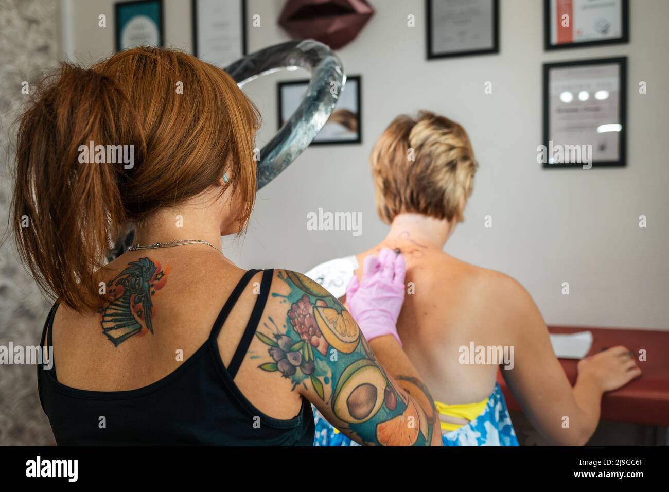Female tattoo-artist makes a tattoo at woman's back. Rear view. Inside ...