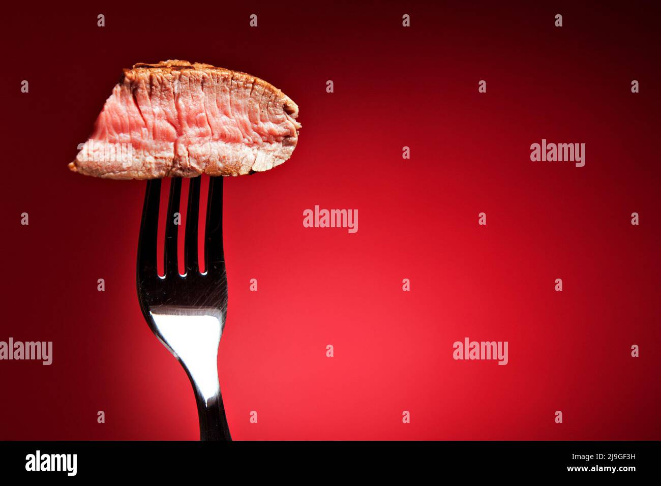 Piece of a grilled steak on a fork isolated on red Stock Photo - Alamy