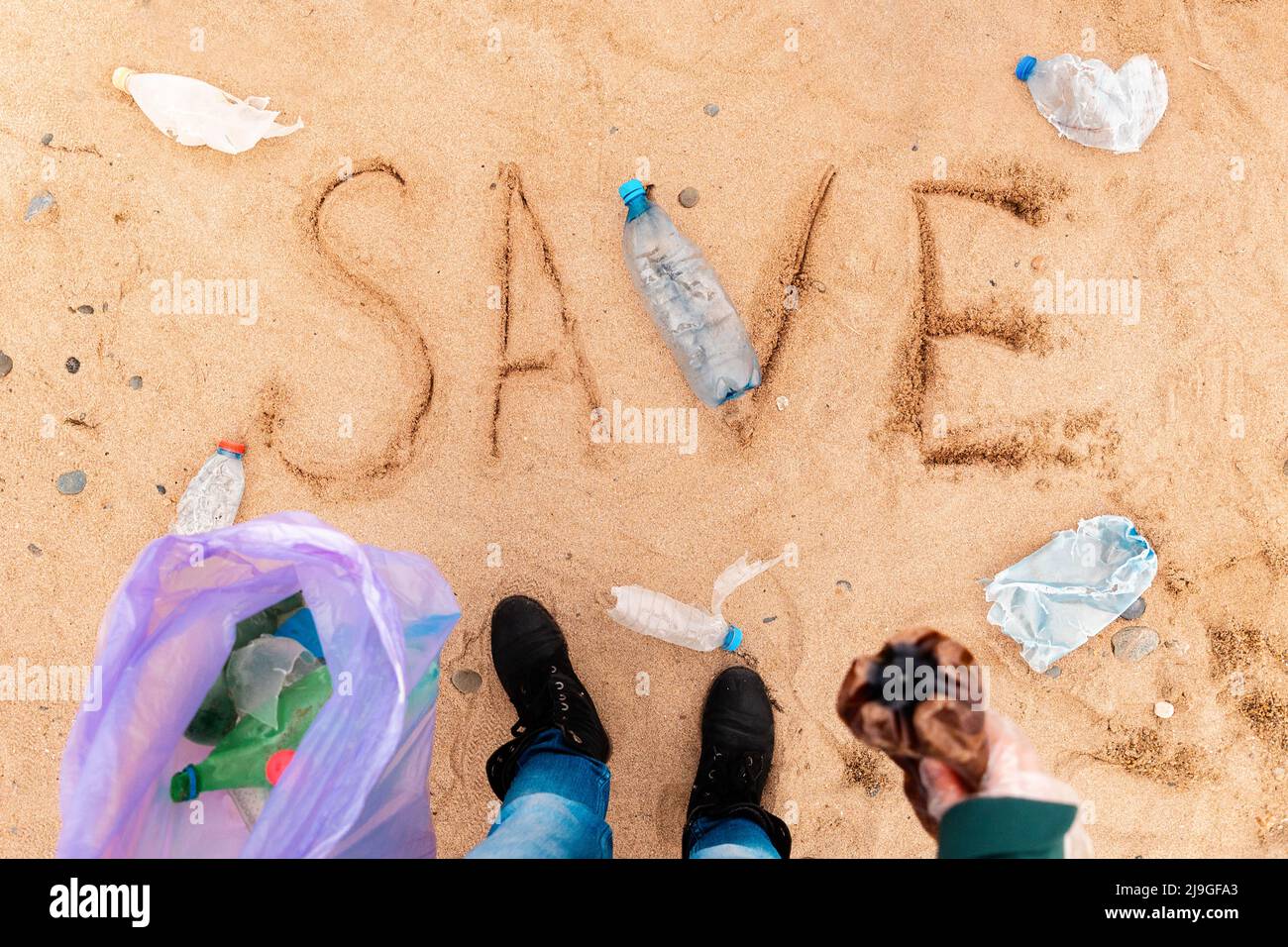 Volunteer stands on a sandy beach with trash bag. Text SAVE on coast ...